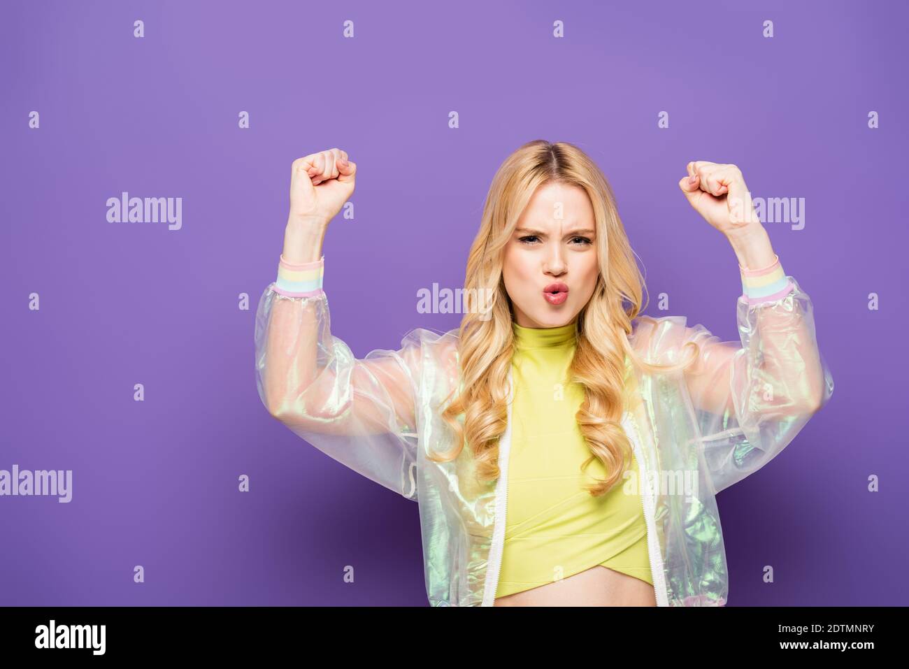 blonde young woman in colorful outfit showing yeah gesture on purple ...