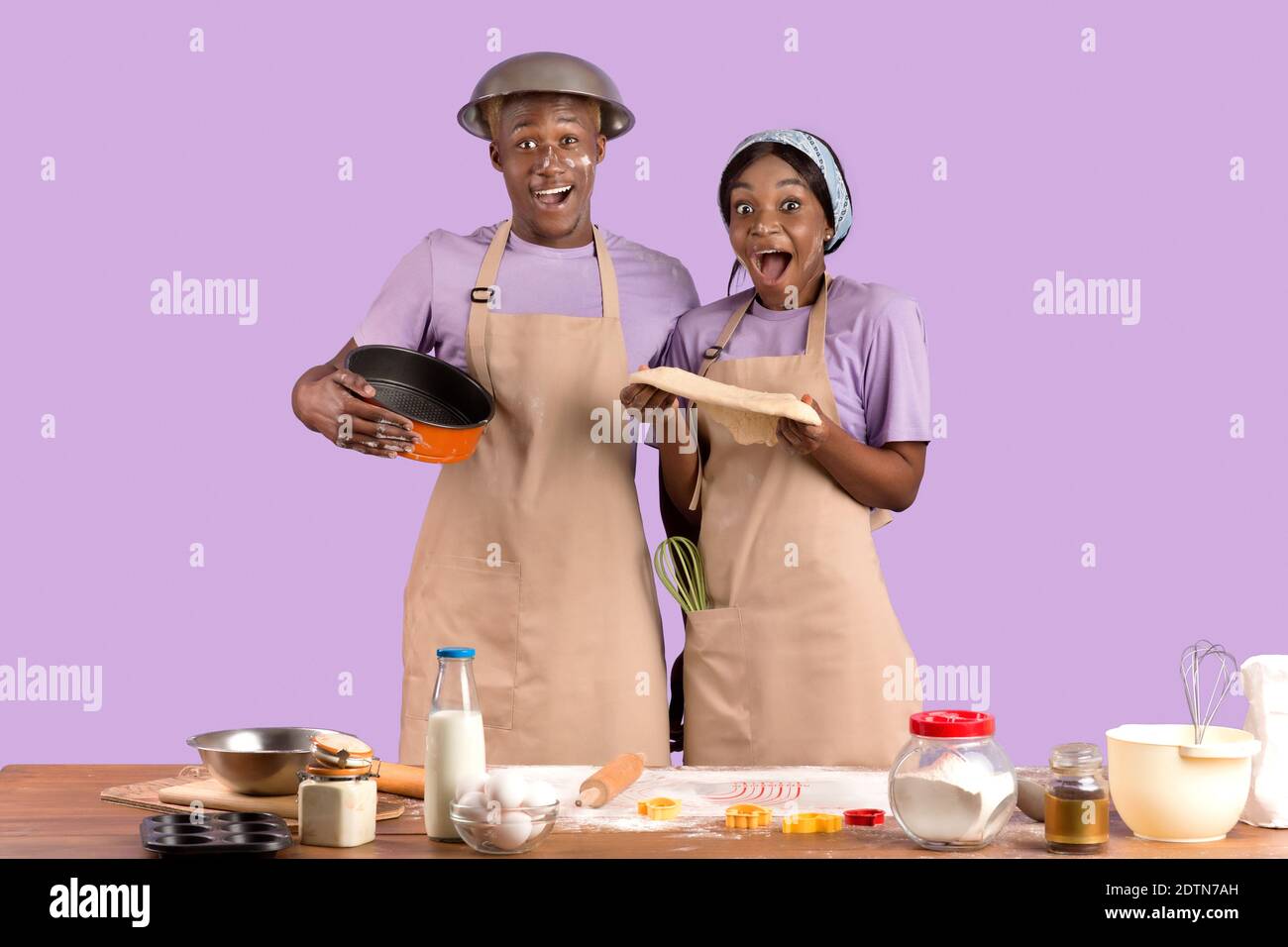 Excited black couple cooking together, holding homemade dough on violet ...