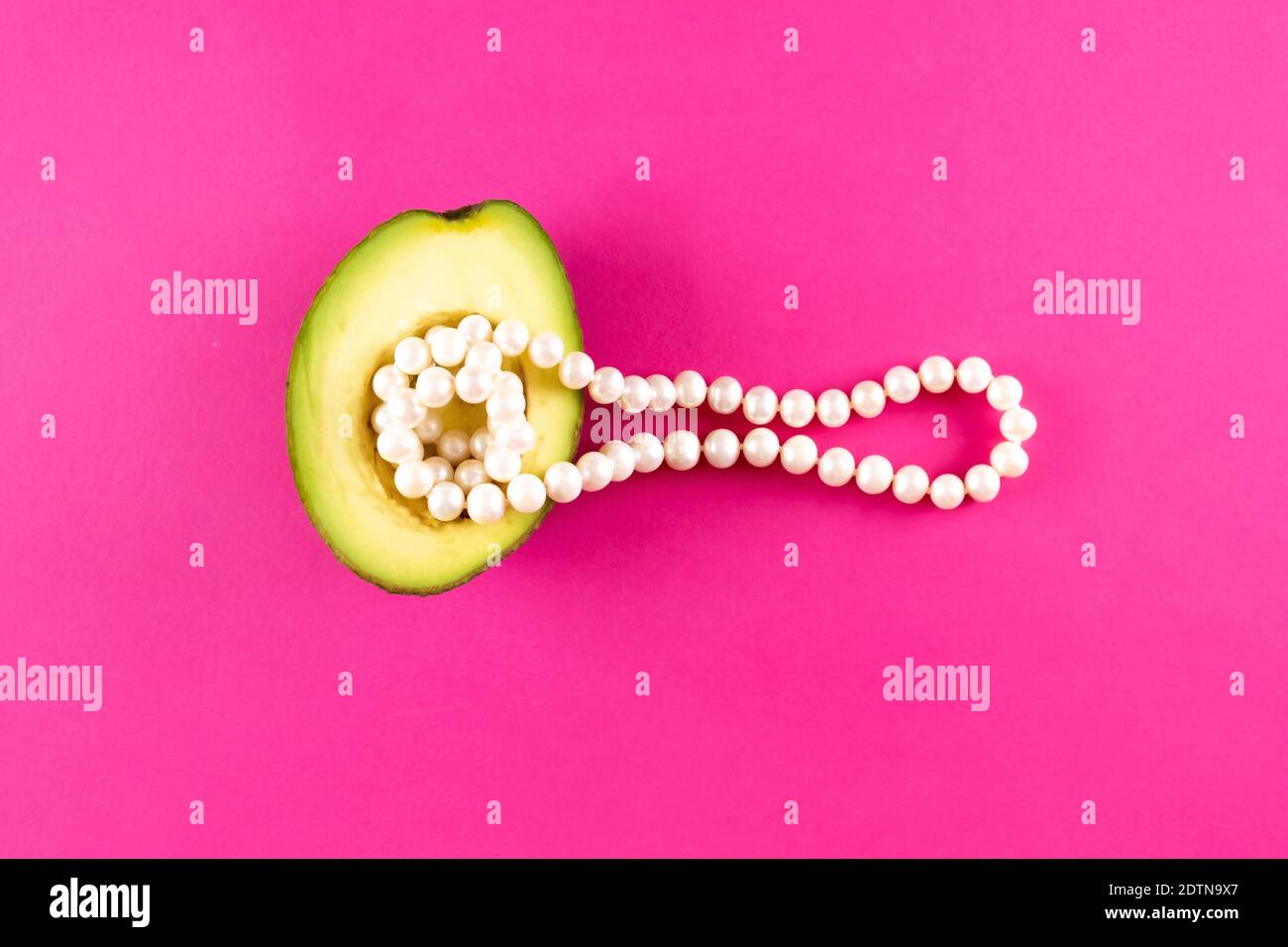 half an avocado with pearls on a light pink background. idea of womens ...