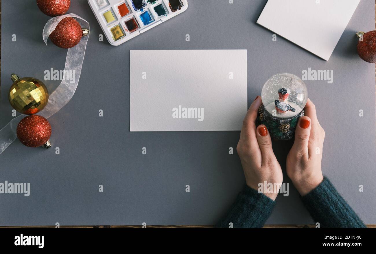 Female hand holding a snow globe near clean white paper. Text rady ...