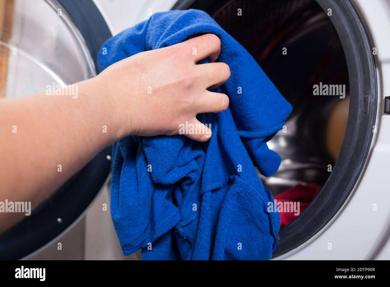 Woman's hand load a washing machine with blue colour clothes Stock ...