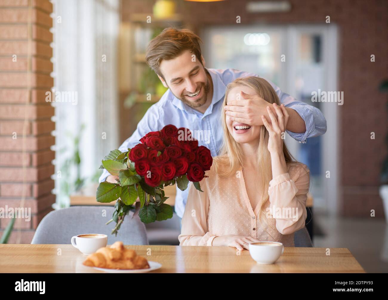 Romantic surprise. Affectionate young man giving bouquet of flowers to ...