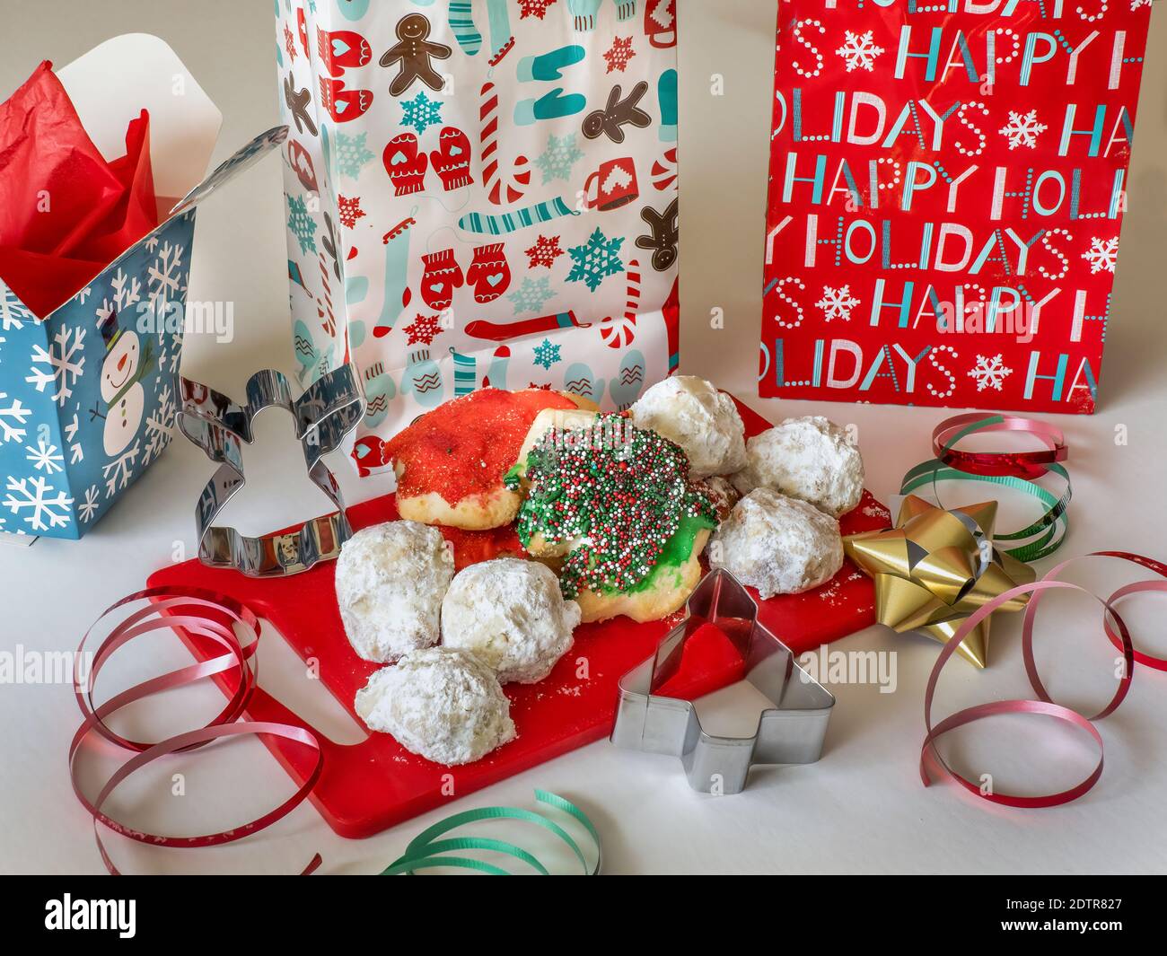 Assorted Christmas cookies on a red cutting board with holiday packages ...