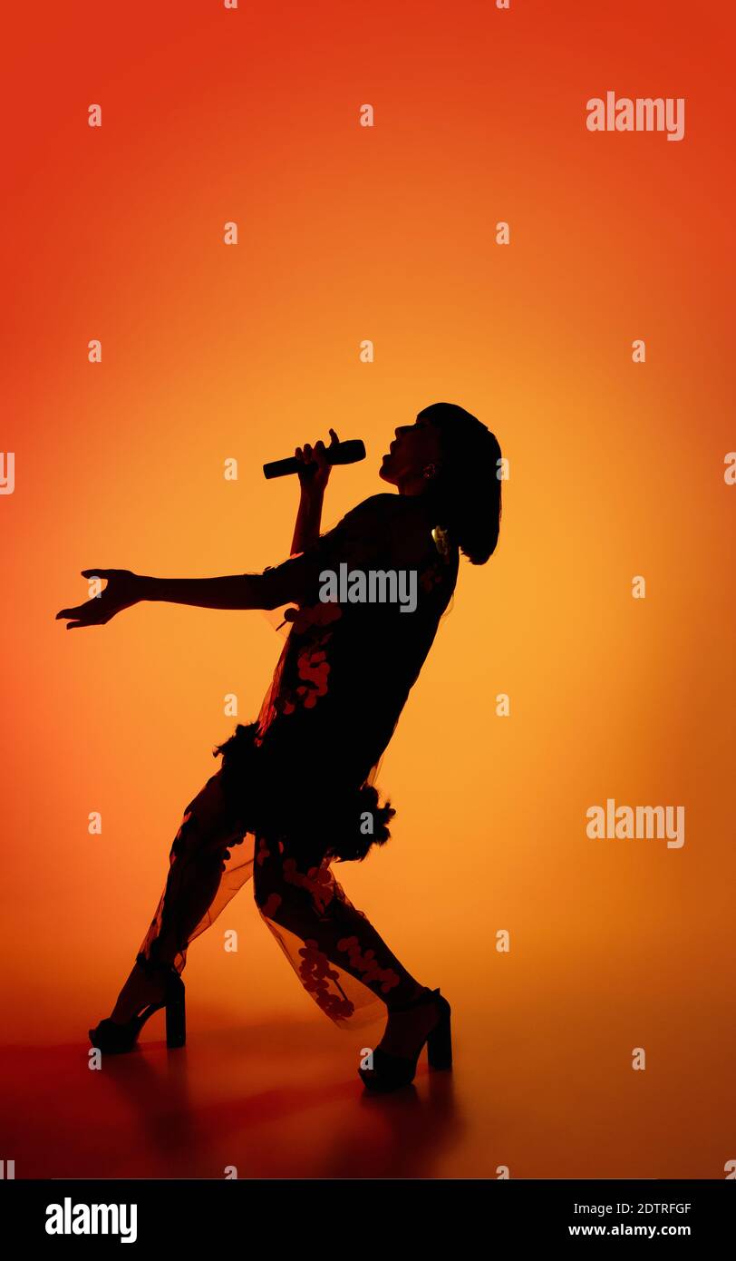 Dance. Silhouette of young female singer isolated on orange gradient ...