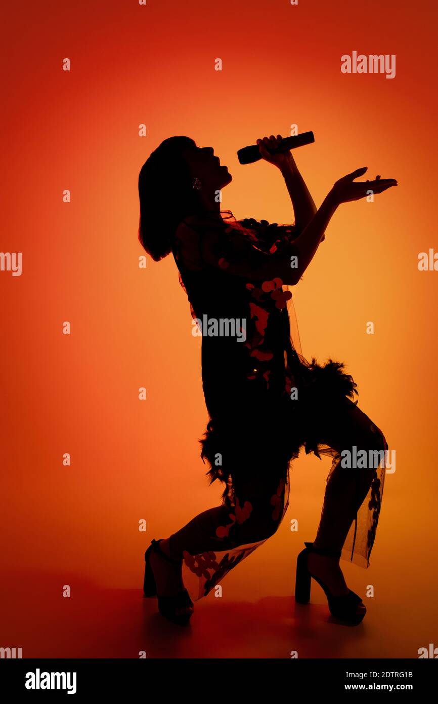 Night. Silhouette of young female singer isolated on orange gradient ...