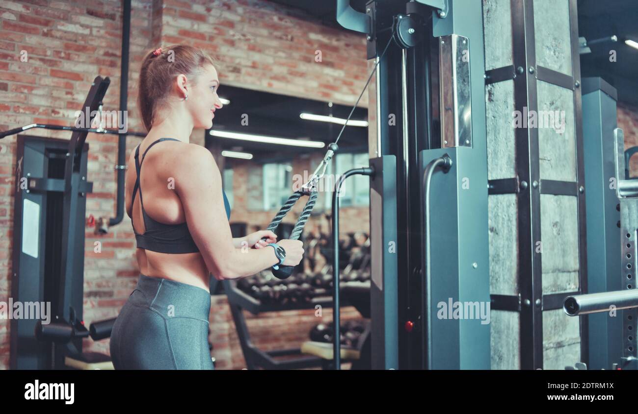 Sportswoman doing exercise on triceps with pulldown station on gym ...