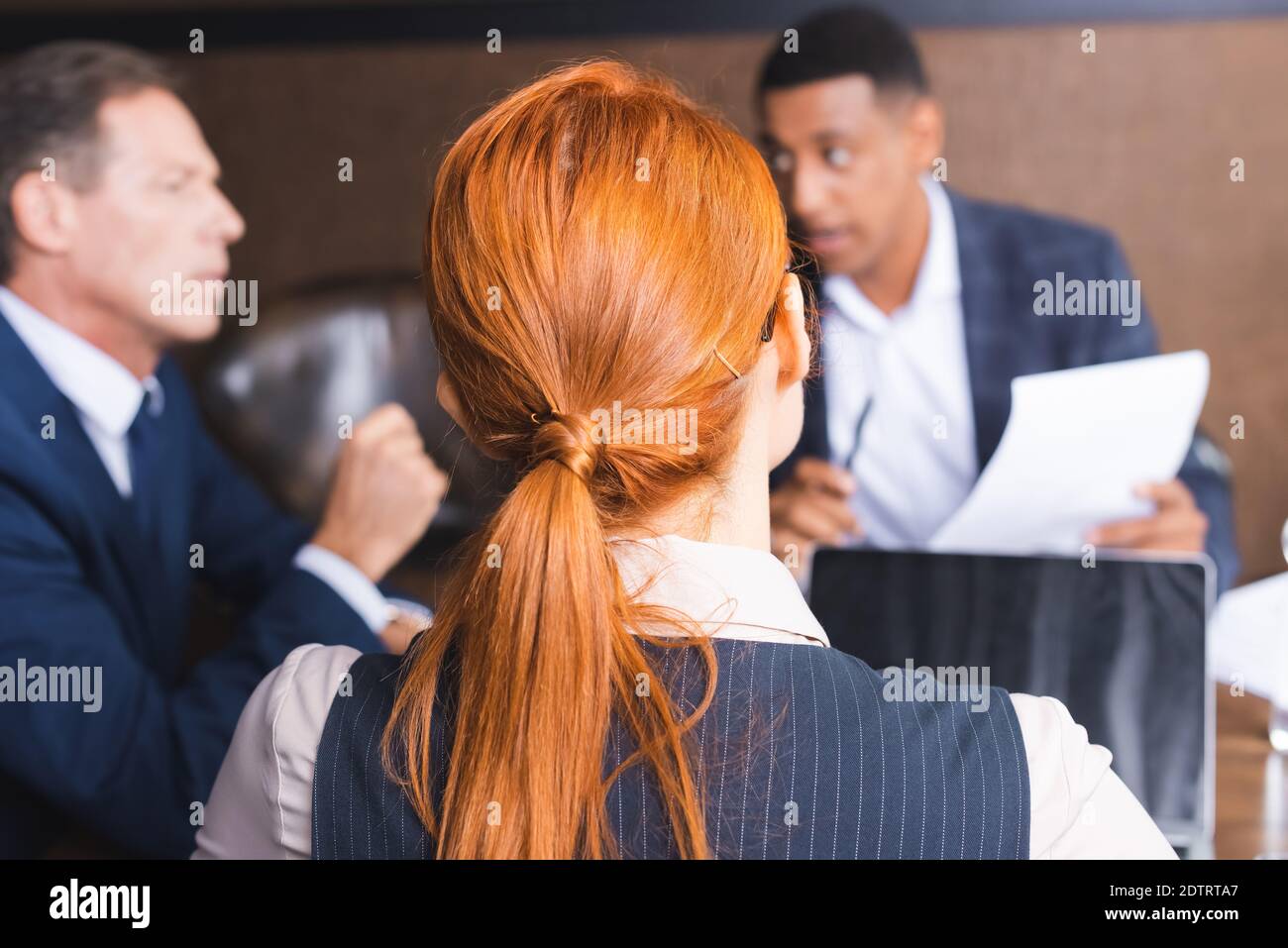 Back view of redhead businesswoman with blurred colleagues discussing ...