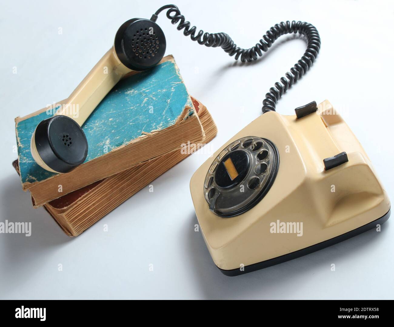 Retro rotary phone and a stack of old phone books on white background ...