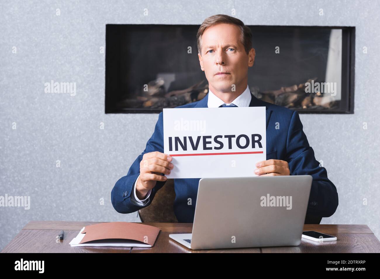 Serious businessman looking at camera and holding sign with investor ...