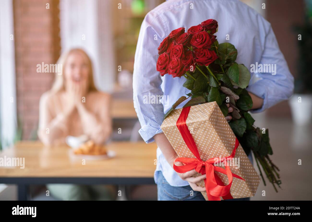 Unrecognizable young guy hiding gift and bouquet of red roses behind ...