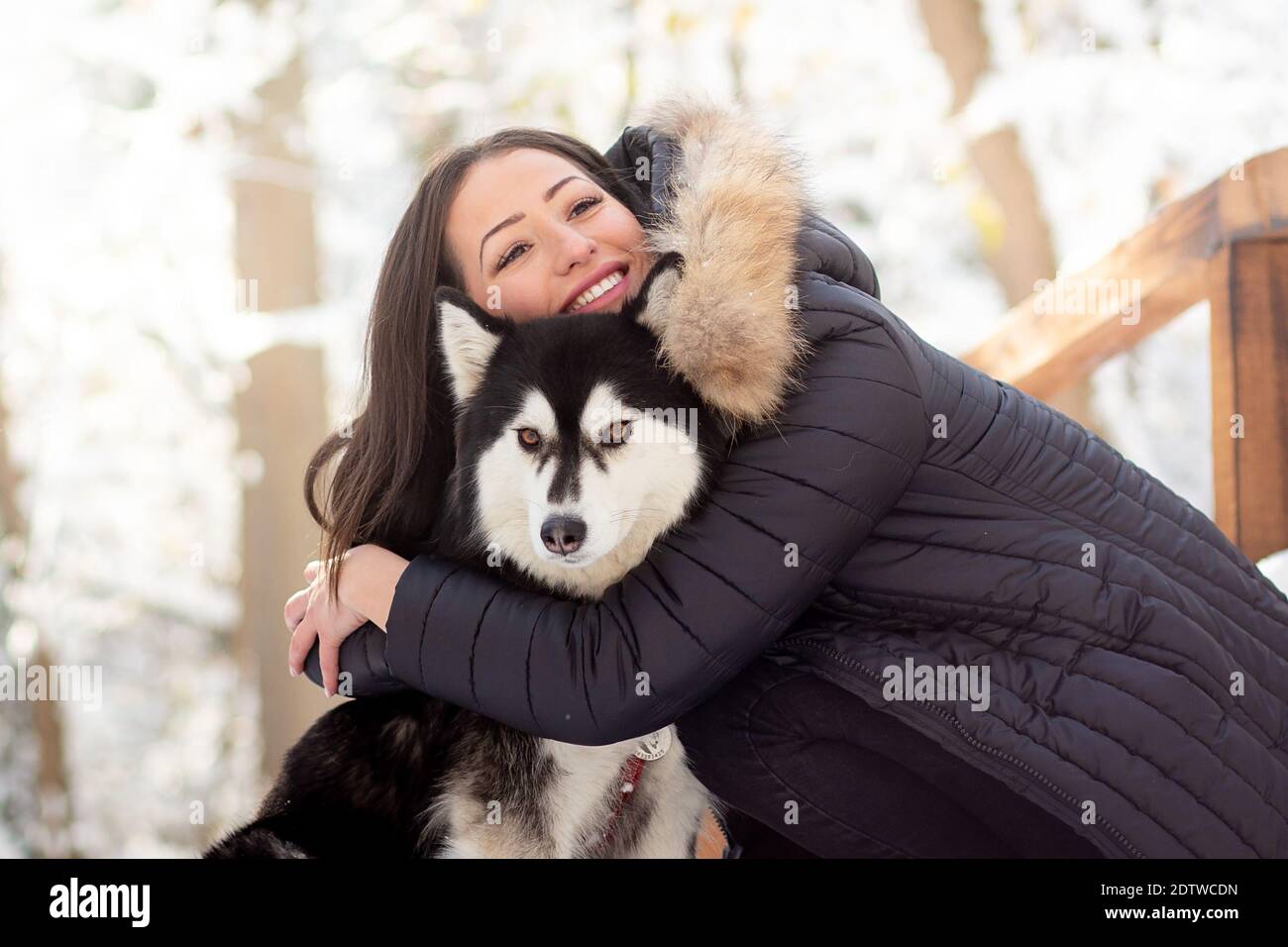 Beautiful young woman hugging female husky dog in cold winter snowy day ...