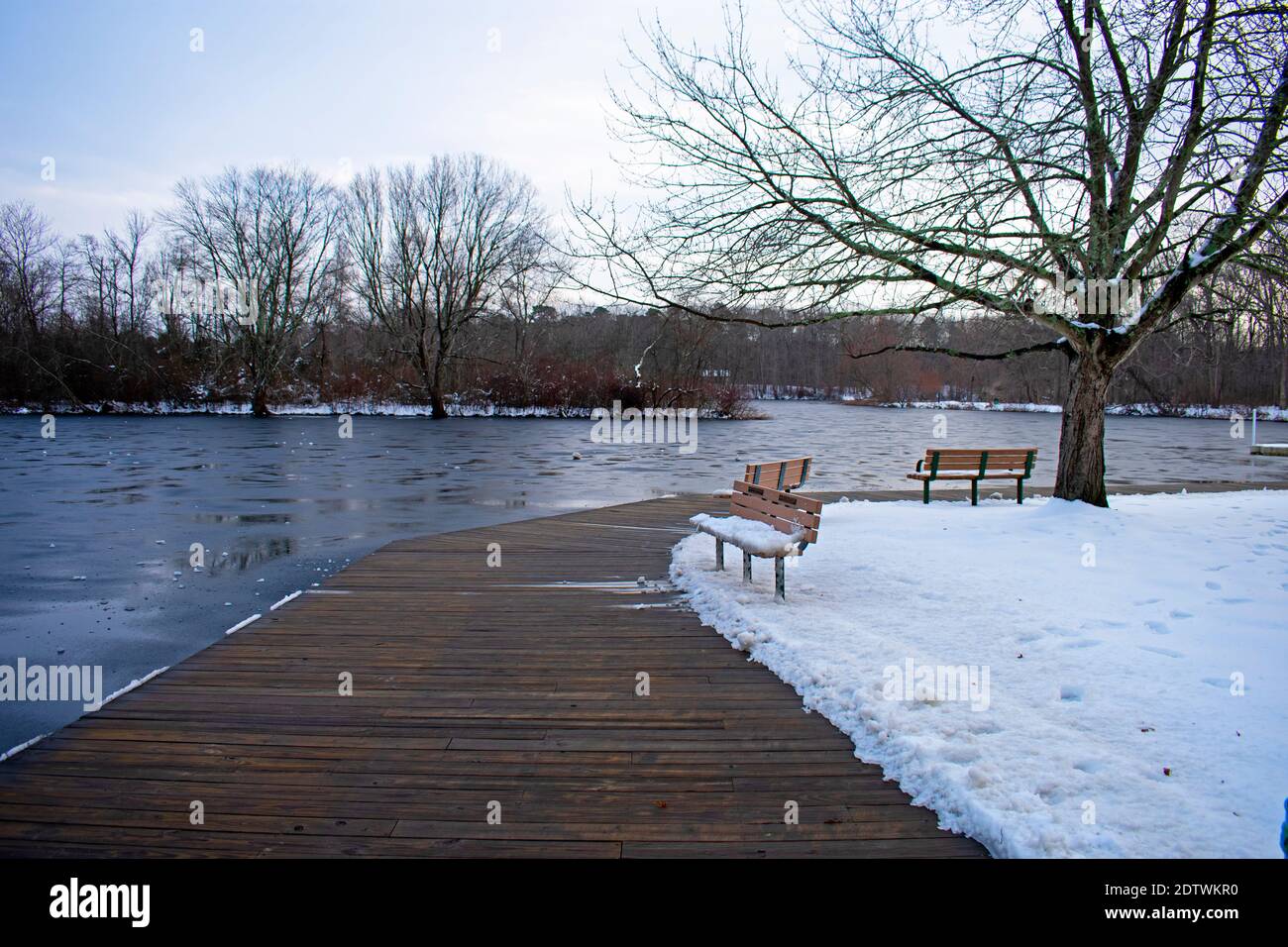 Snow covered wooden benches overlooking thin ice in a small lake at ...