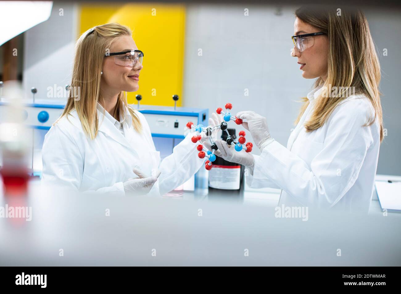 Female chemists with safety goggles hold molecular model in the lab ...