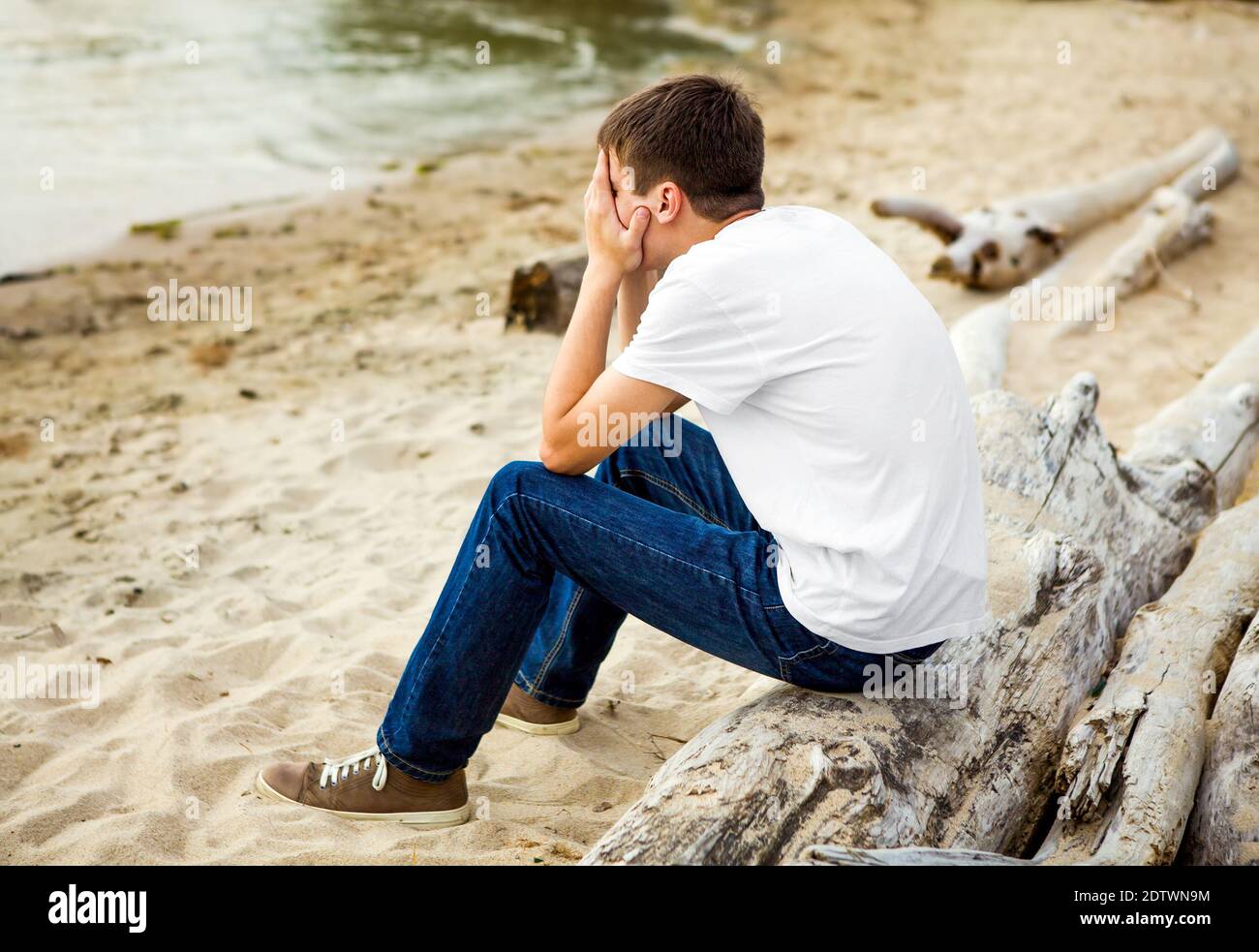 Sad Young Man sit on the Log at the Seaside Stock Photo - Alamy
