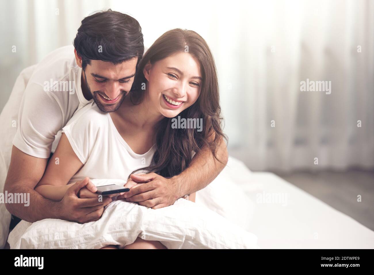 couple using mobile phone on white bed in morning time Stock Photo - Alamy