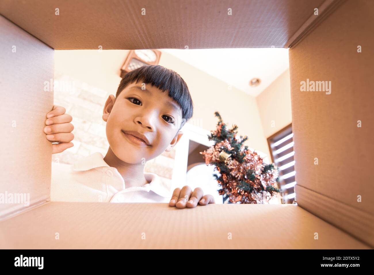 The happy child unpacking, opening the carton box and looking inside ...