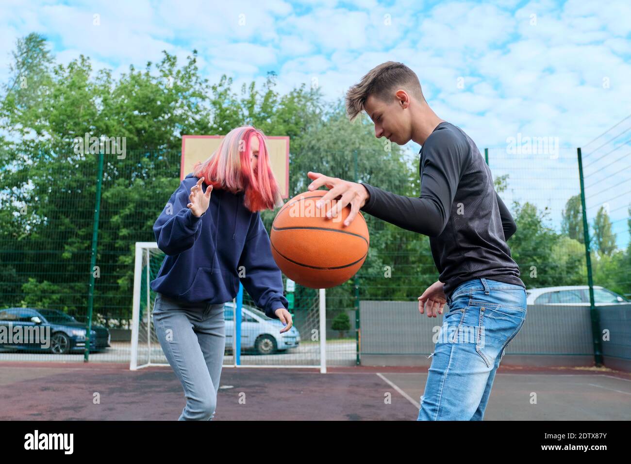 Teenagers guy and girl on an outdoor basketball court playing street ...