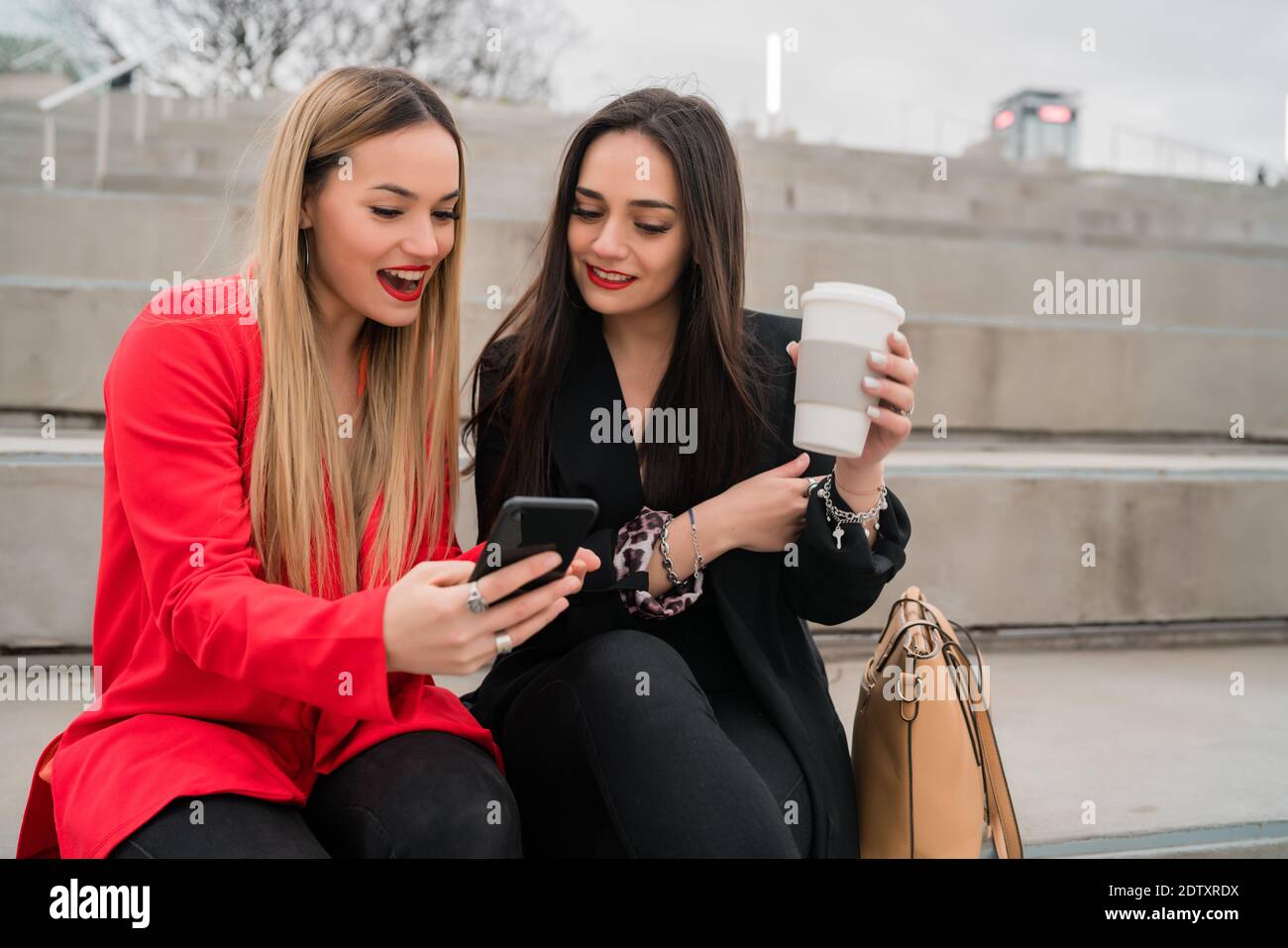 Two friends using their mobile phone while sitting outdoors Stock Photo ...