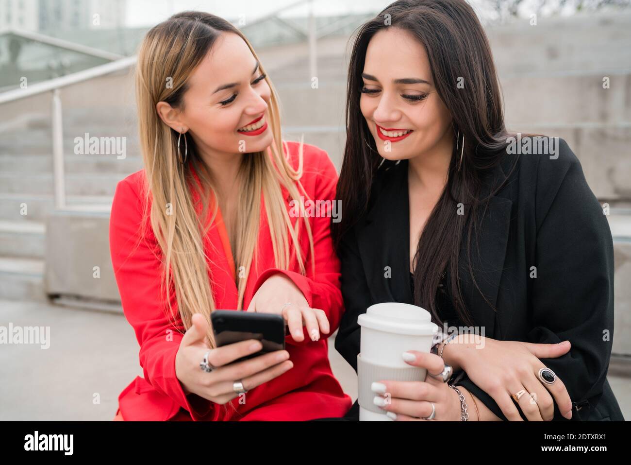 Two friends using their mobile phone while sitting outdoors Stock Photo ...