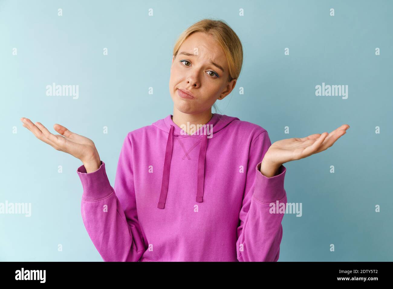Portrait of a young casual woman shrugging shoulders isolated on a blue ...