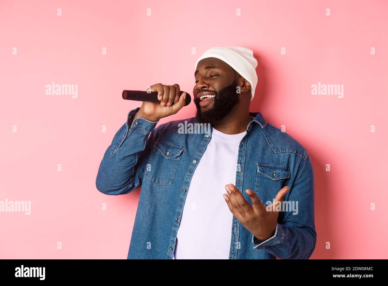 Handsome Black man in beanie and denim shirt singing karaoke, holding ...