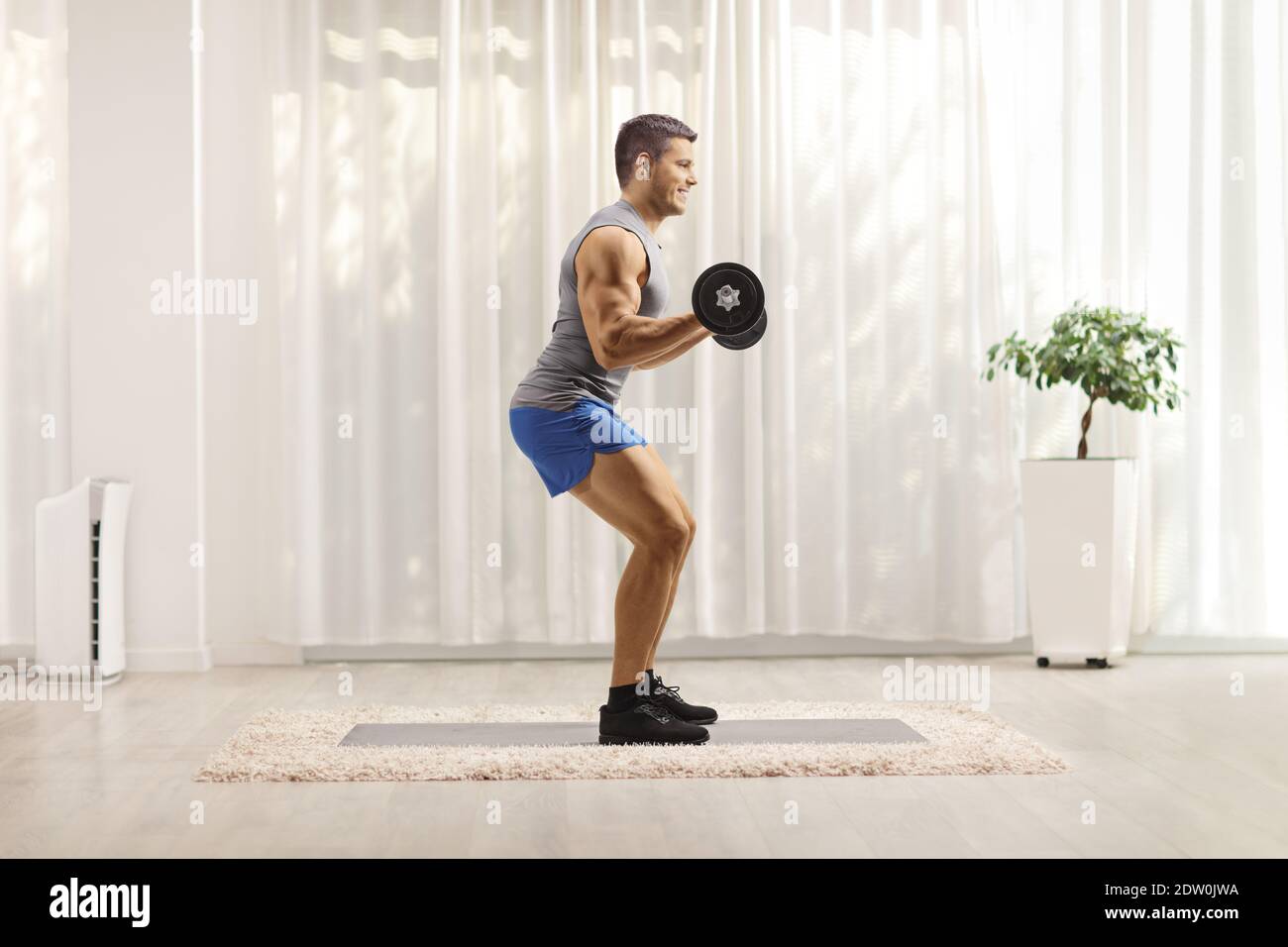 Full length profile shot of a young man bodybuilder lifting weights at ...