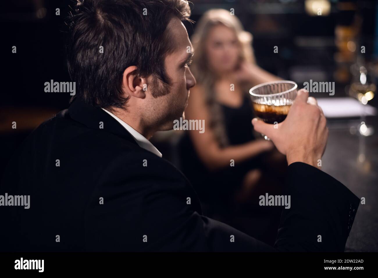 a young man in a suit drinks whiskey with coke and ice at the bar in a ...