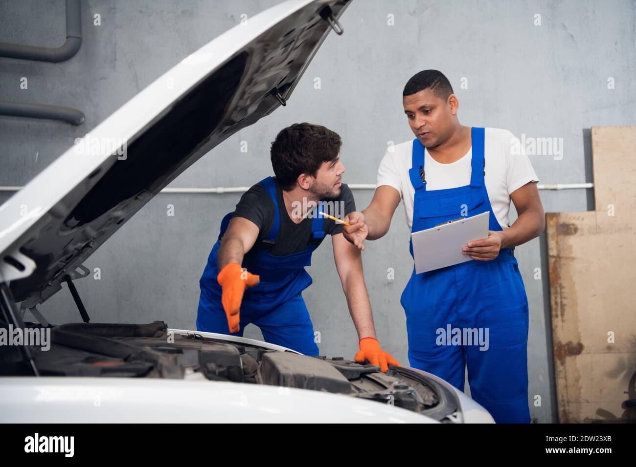 Mechanics inspect the engine of a automobile and discuss repair Stock ...