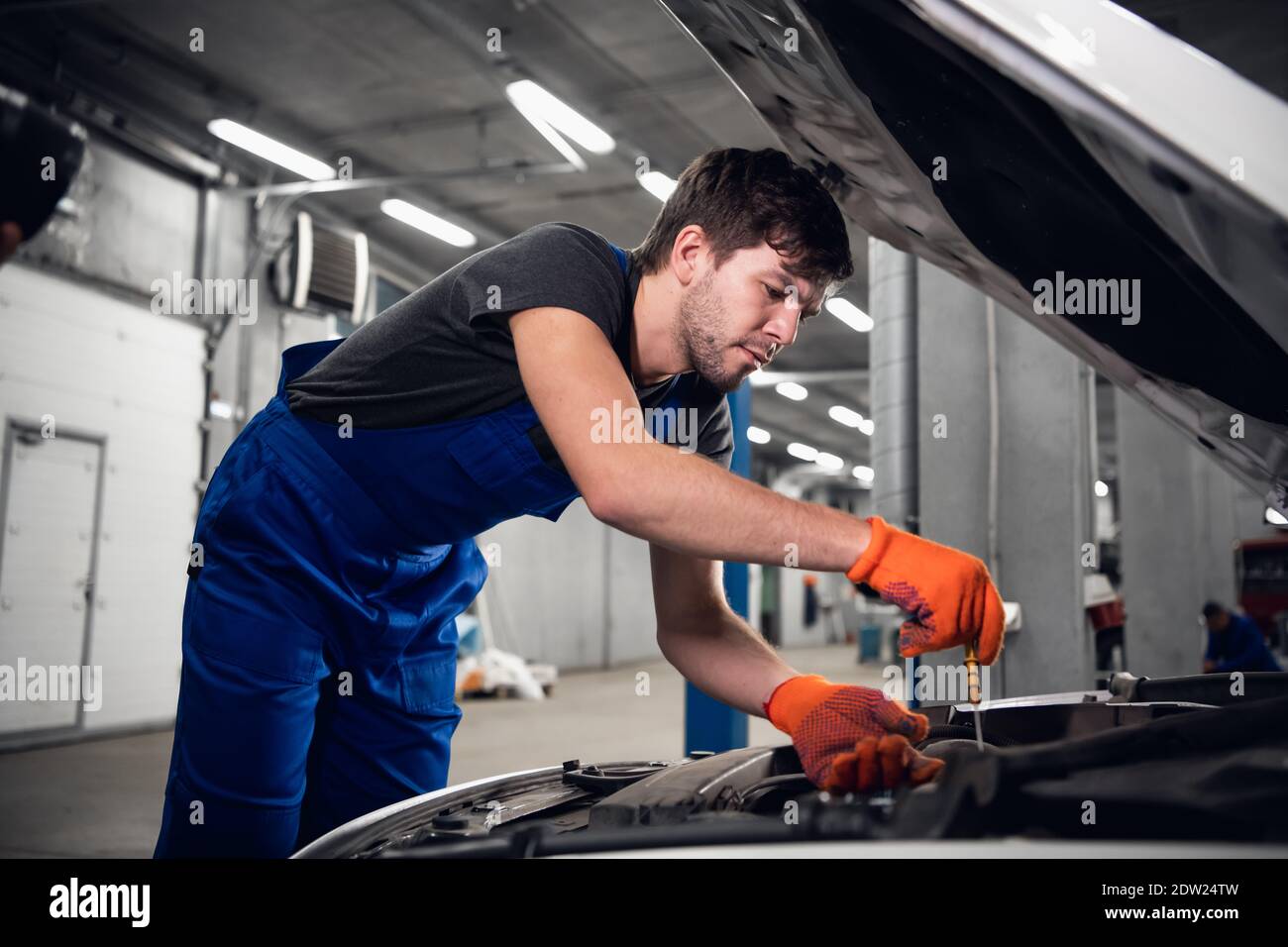 A workman using tools to repair a car engine. He is dressed in blue ...