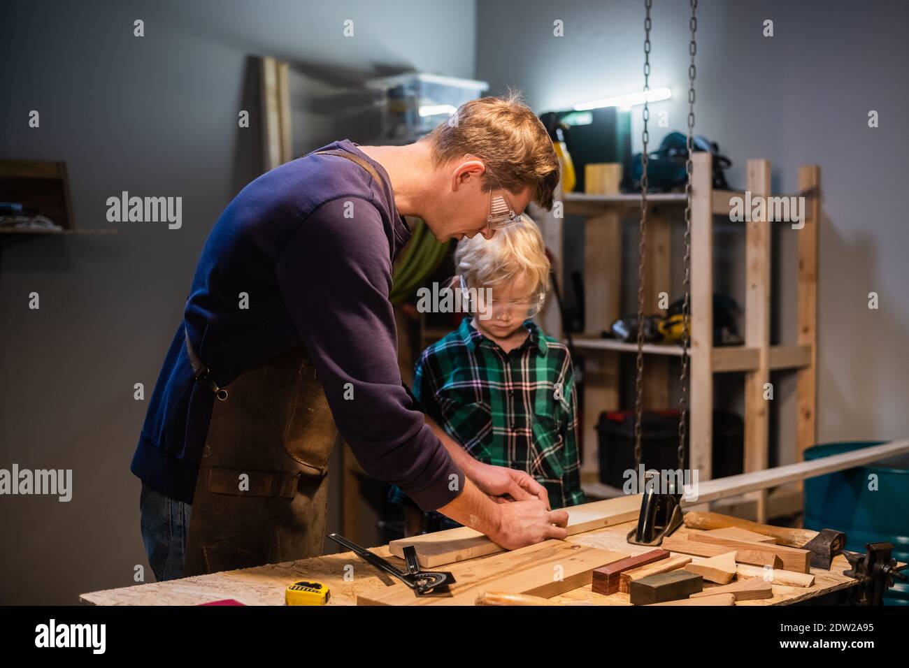 a young father teaches the basics of carpentry to his son in the garage ...