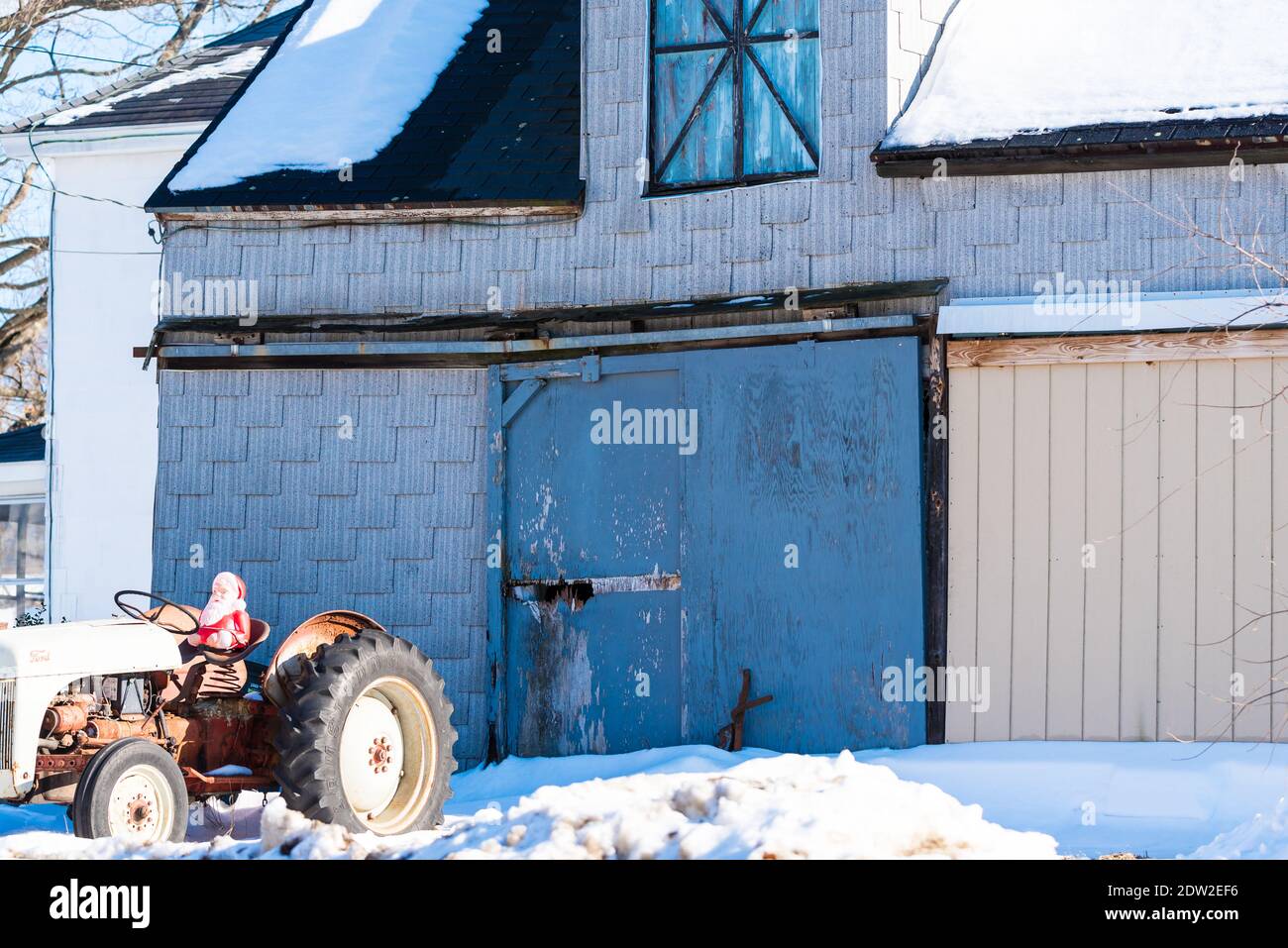 Toy Santa Claus sitting on a farm tractor in front os an old ...