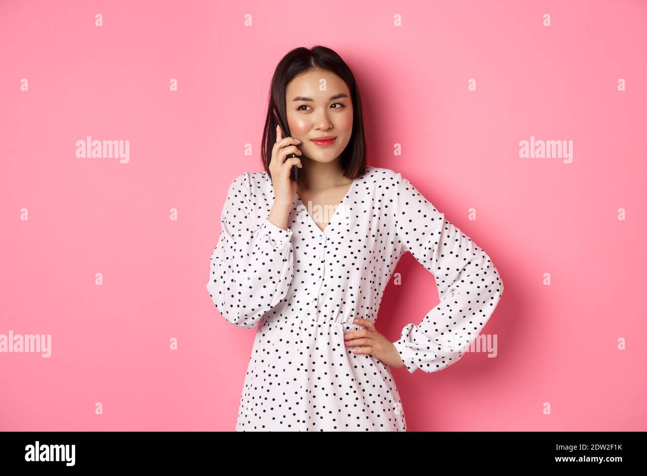 Attractive korean woman making a phone call, holding smartphone near ...