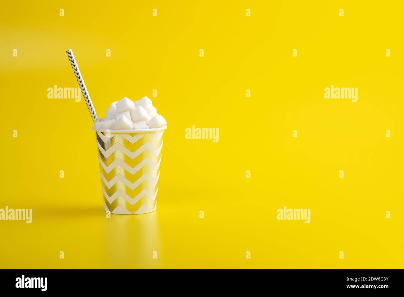 Straw in disposable paper cup filled with sugar cubes over yellow ...