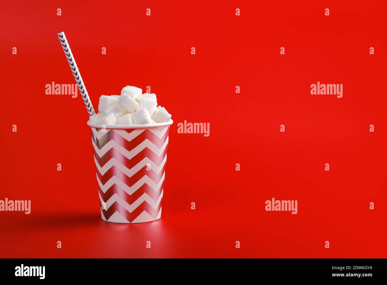 Straw in disposable paper cup filled with sugar cubes over red ...