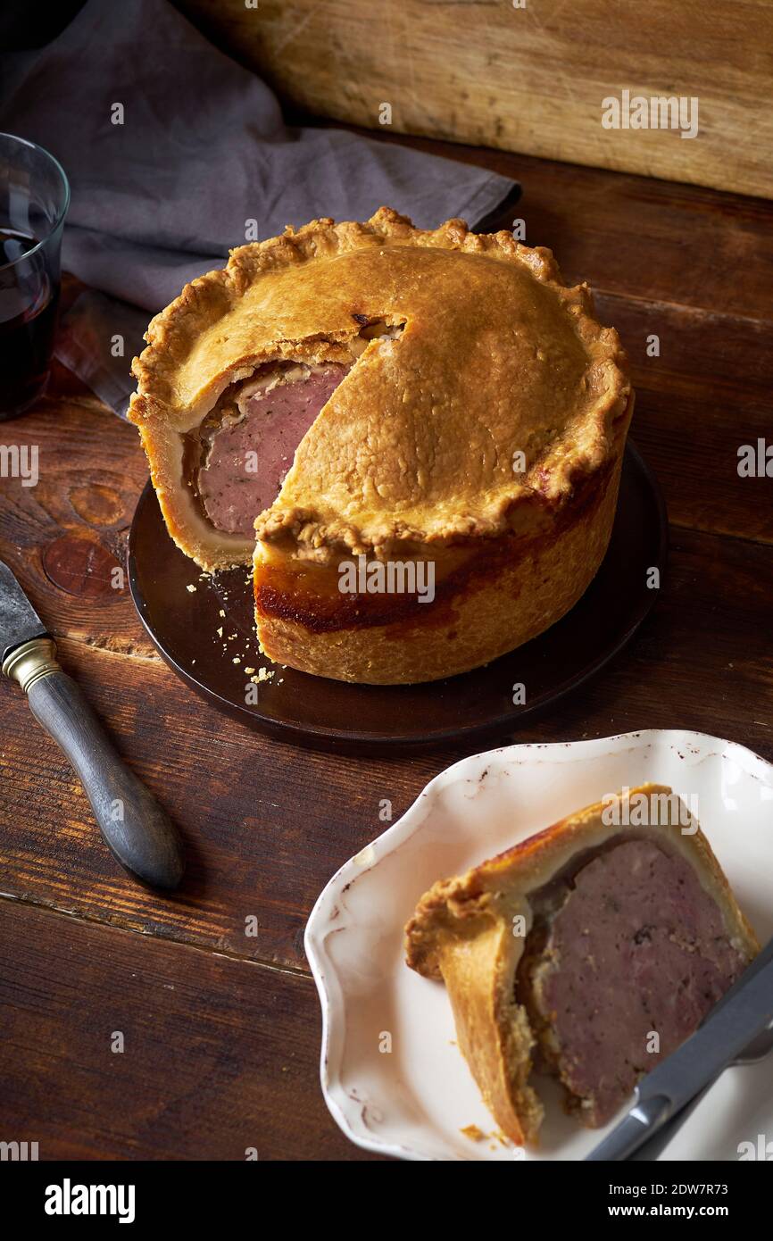 Traditional british raised pork pie with bacon and herbs with one slice ...