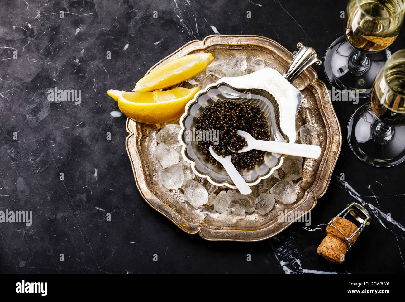 Black caviar in silver bowl and Champagne on black marble background ...
