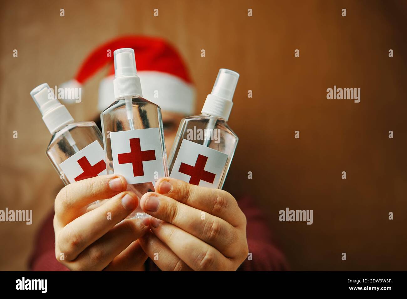 Sanitizers with red cross on label in hands. Man in red Santa hat ...