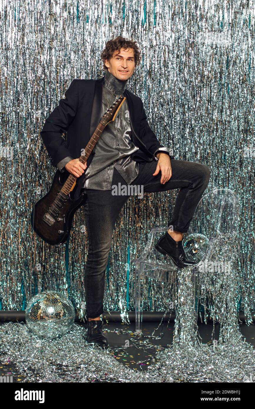 Tall attractive man holding electro guitar standing over the sparkle ...