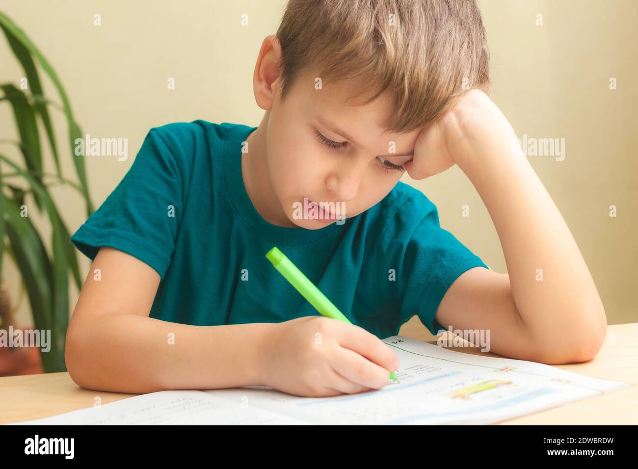 7 yeas old boy sitting at desk and doing homework. Child write notes in ...