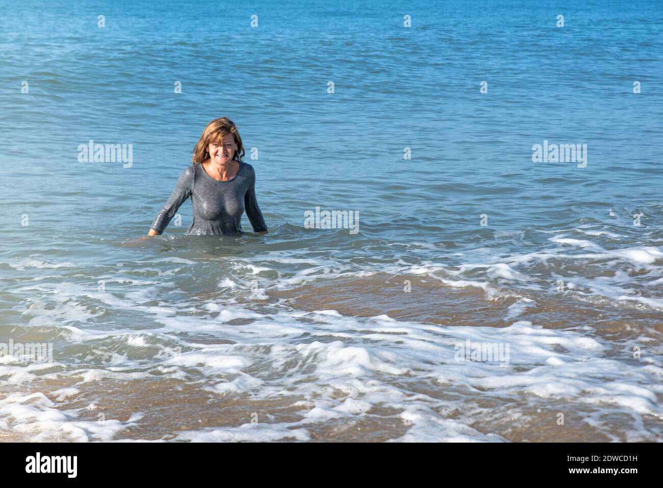Woman coming out of the sea in a wet dress after a swim at the beach ...