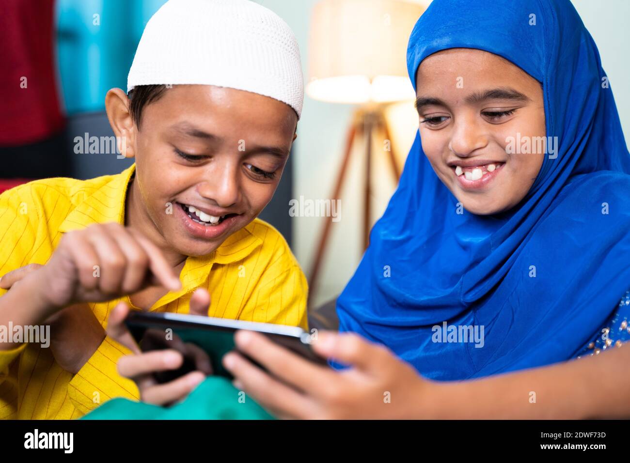 Two muslim sibling kids busy using mobile at home - concept of kids ...