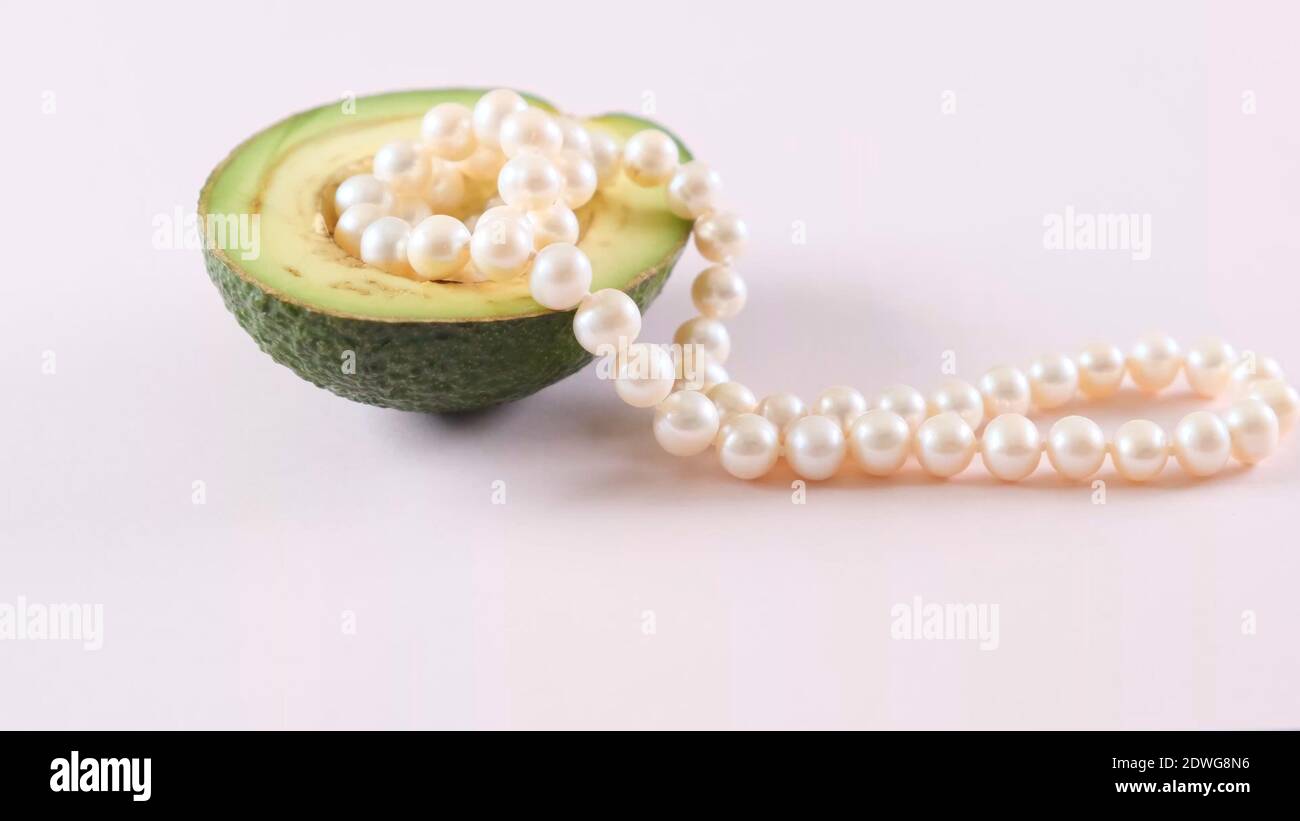 half an avocado with pearls on a light pink background. surrealism ...