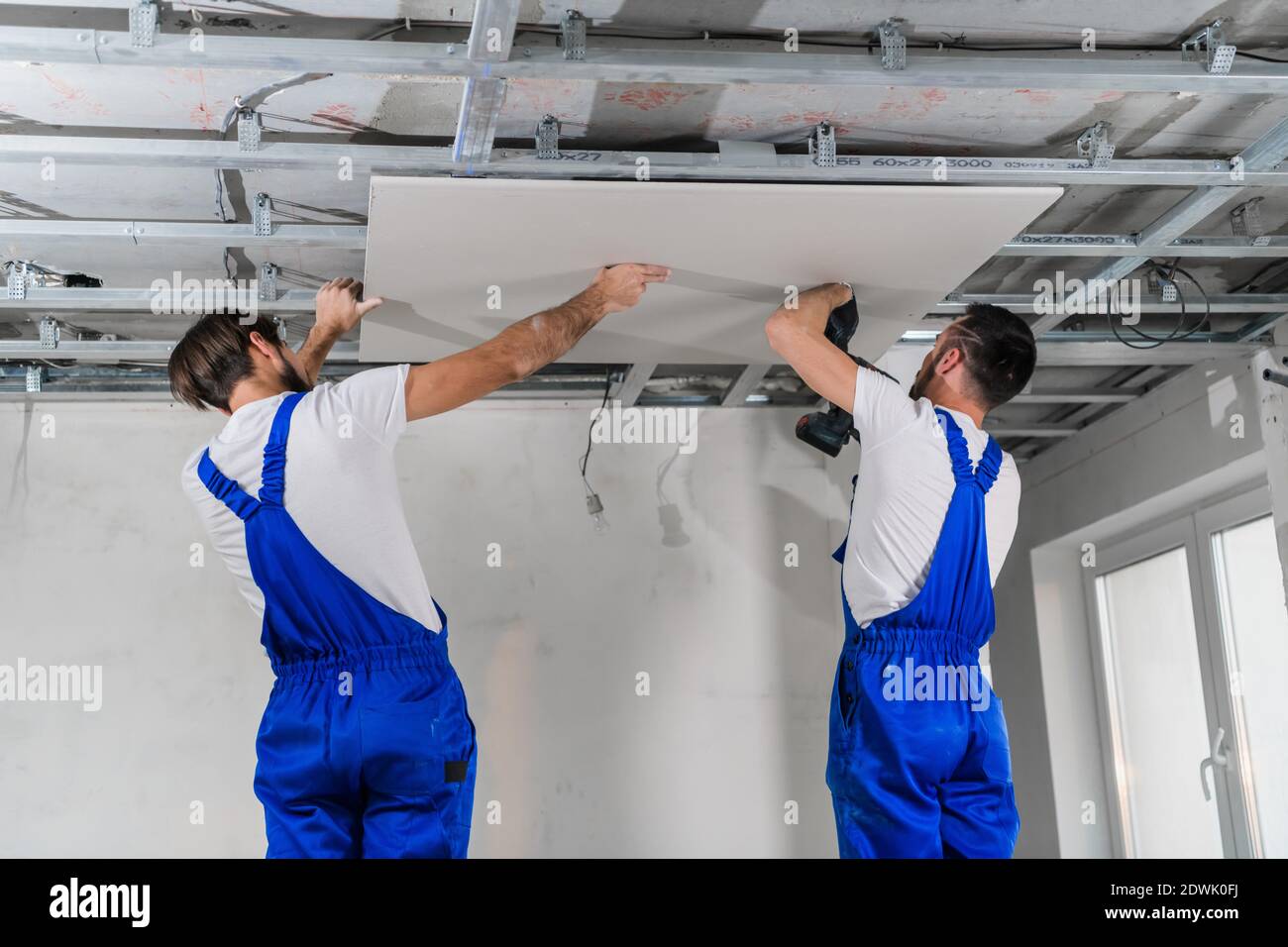 Builders in blue overalls stand on a ladder and make a ceiling Stock ...