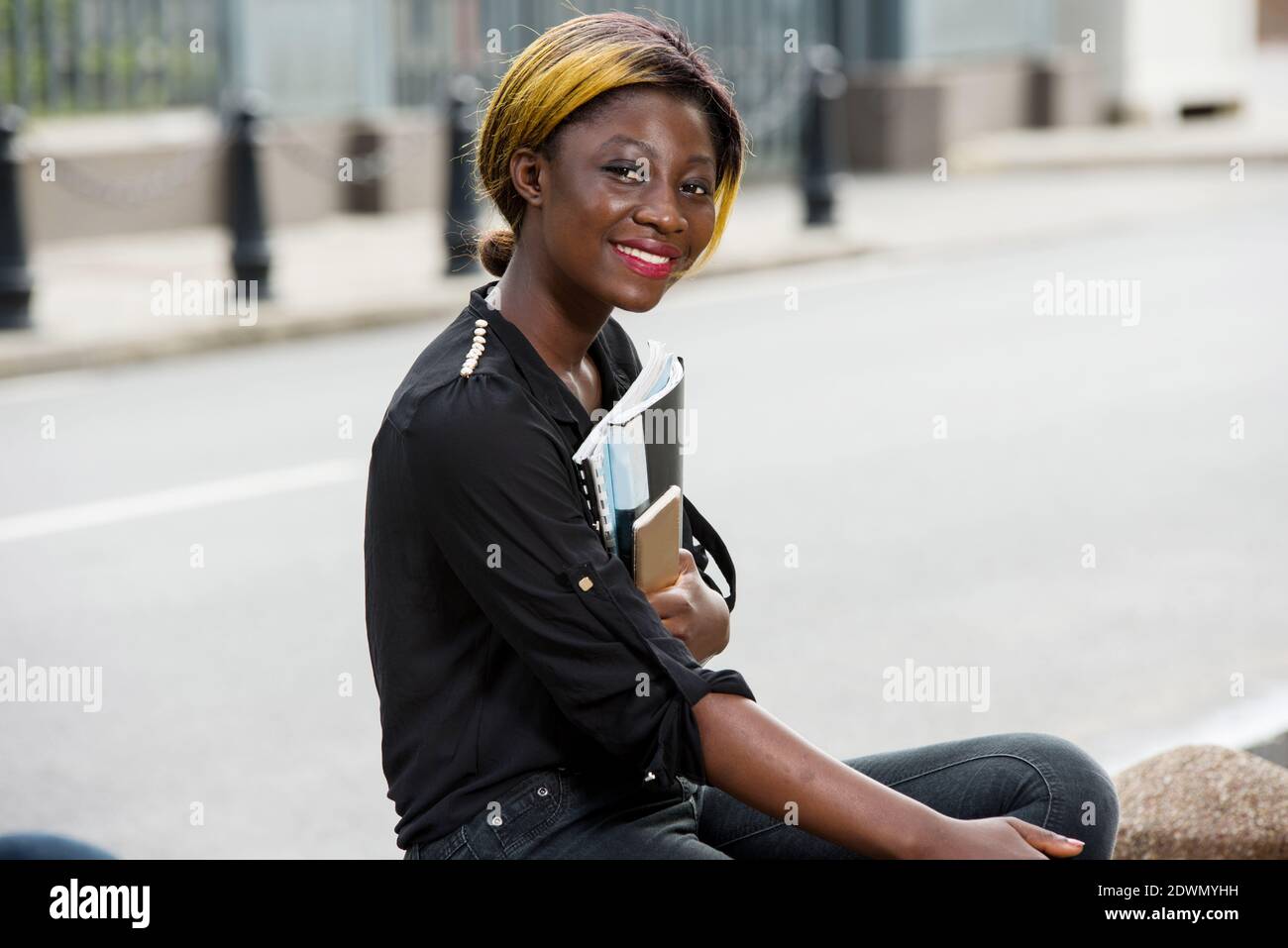 happy university student sitting alone outdoors holding books Stock ...