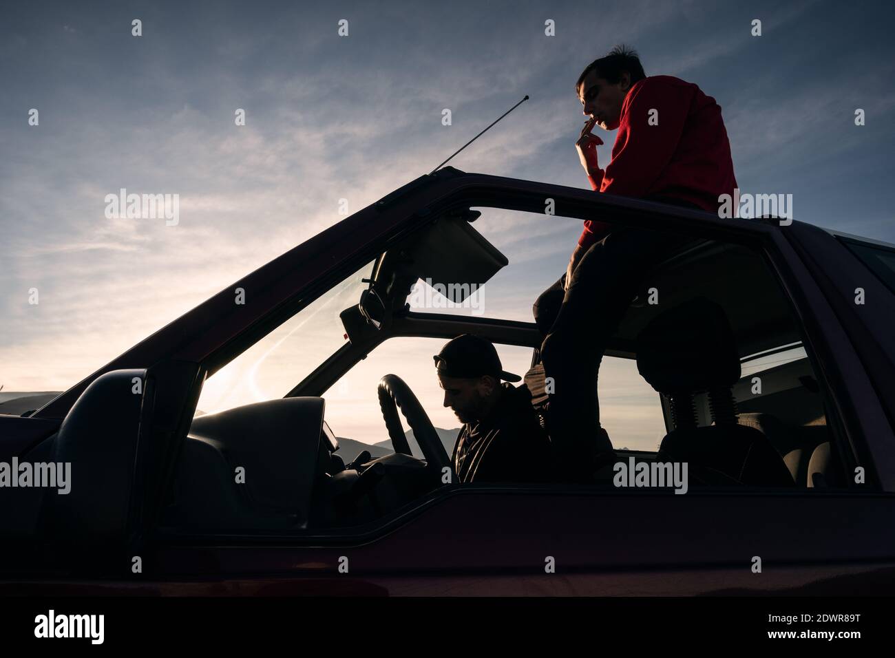 Two friends enjoying the sunset on the rooftop of a convertible off ...