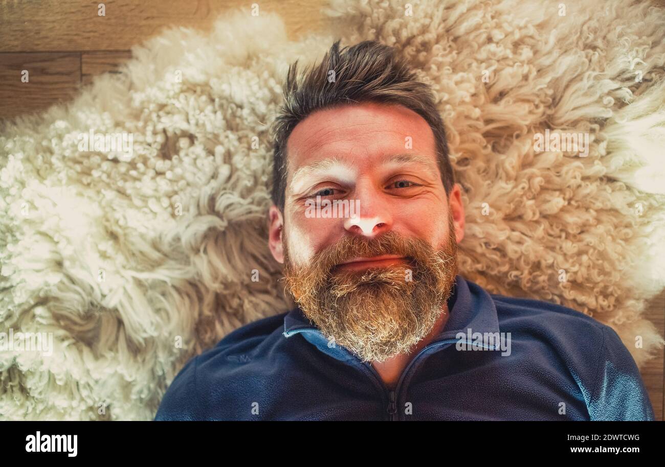 portrait of happy relaxed man laying on sheepskin rug Stock Photo - Alamy