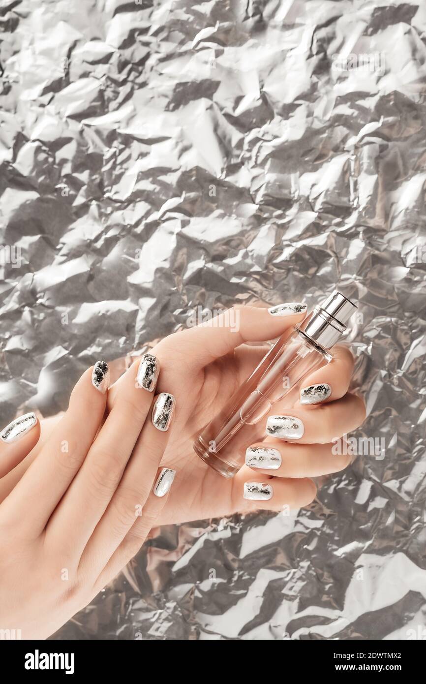 Female hands with trendy silver nail design holding stylish bottle of ...
