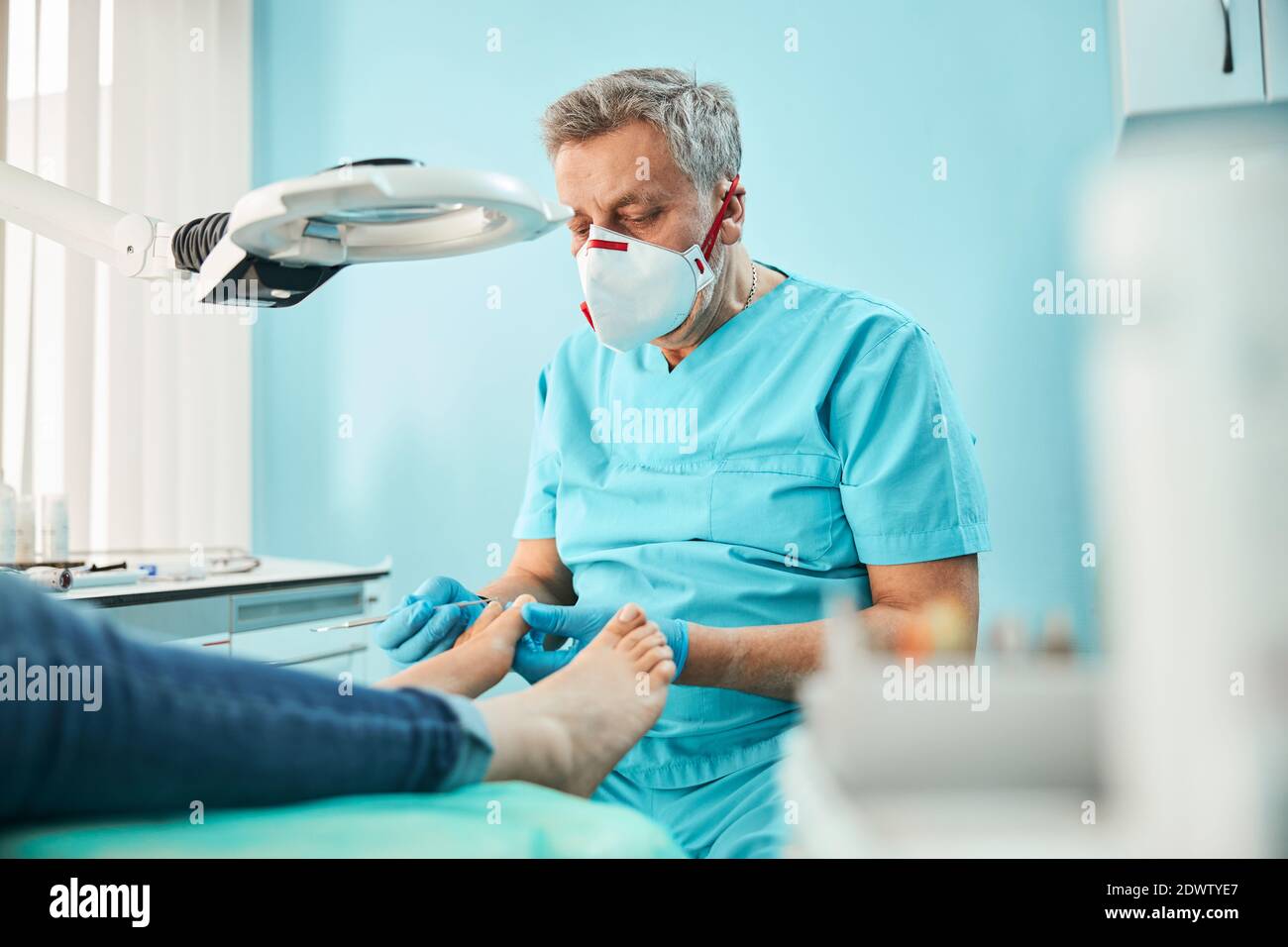 Chiropodist podiatrist in blue uniform and gloves with medical tool in ...
