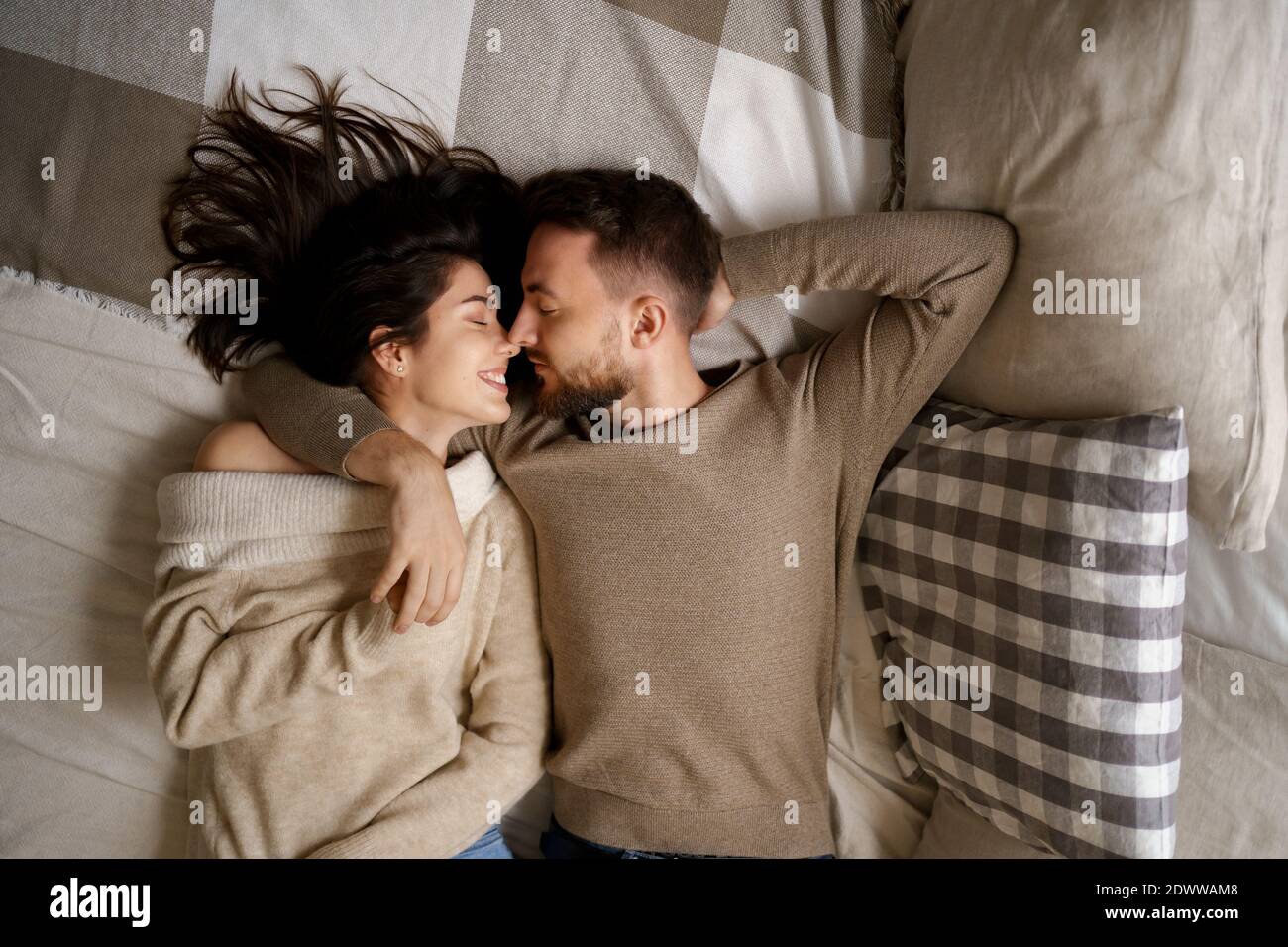 Beautiful young happy couple relaxing in bed and smiling, embracing ...