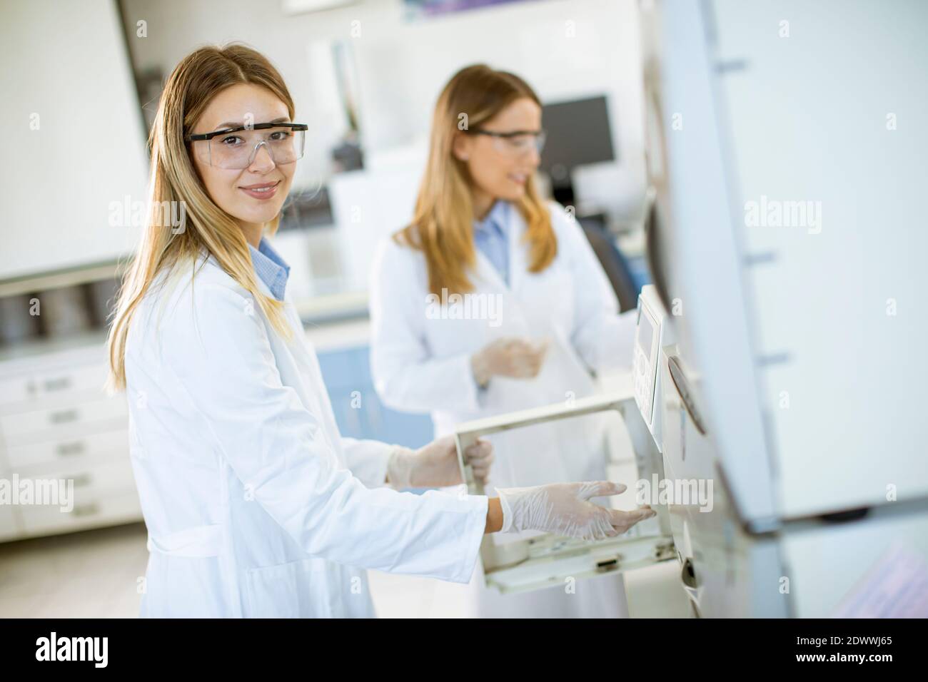 Young female scientists in a white lab coat putting vial with a sample ...